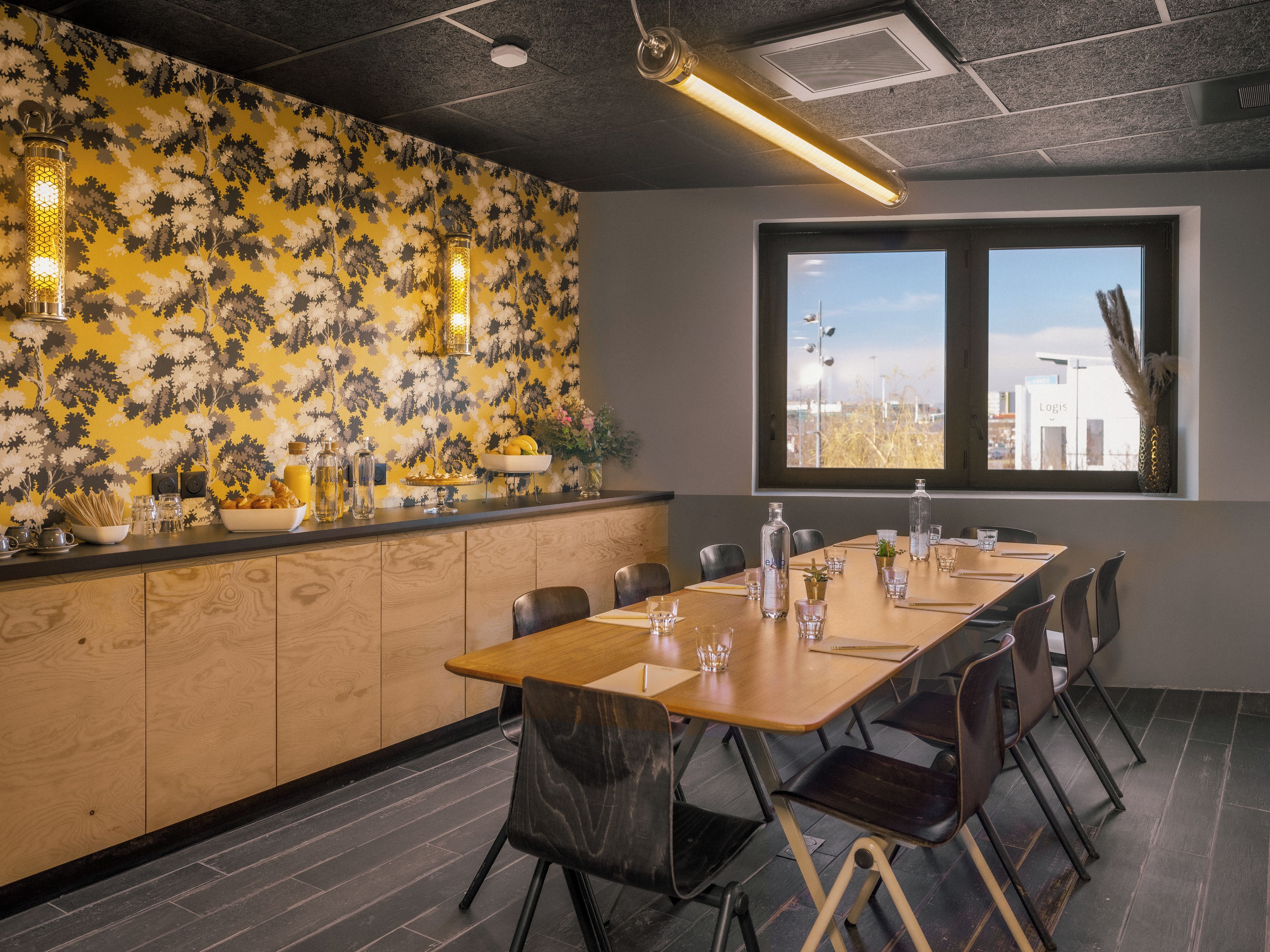 Uma sala de conferência com uma mesa comprida, cadeiras, um armário de madeira e um papel de parede floral.