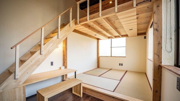 Um quarto japonês tradicional com tatames, escada de madeira e um pequeno banco.