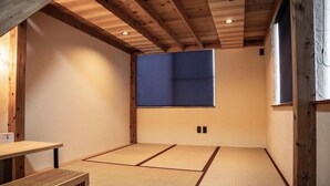 Um espaço com tatames, teto de madeira, uma janela e uma pequena mesa.