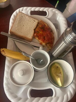 Uma bandeja com torradas, uma fatia de pizza, um saleiro, uma colher, uma tigela pequena e meio abacate.