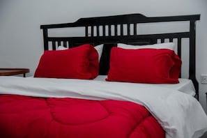 Uma cama com cabeceira preta, almofadas e manta vermelhas.