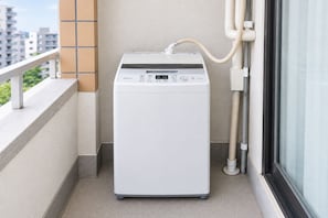 Máquina de lavar roupa compacta e branca numa varanda, com vista para a cidade.