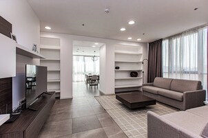 Uma sala de estar moderna com televisão de tela plana, sofá, mesa de centro e um espaço de refeições ao fundo.