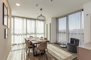 Quarto de hotel moderno com área de refeições, grandes janelas e vista para a cidade.