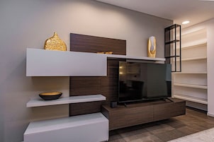 Uma sala de estar moderna com televisão de tela plana, prateleiras de madeira e um objeto decorativo dourado.