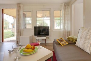 Uma sala de estar com sofá, televisão, mesa de jantar com uma travessa de frutas e um copo, e uma revista.