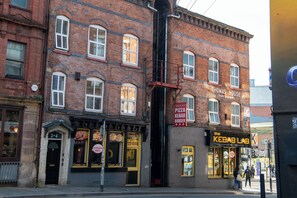 Um edifício de tijolos com várias janelas, uma placa com 'Thomas House' indicando que se trata de um prédio de apartamentos de luxo, e um restaurante 'Kebab Lab' com cardápio visível.