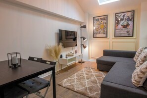 Uma sala de estar moderna com um sofá, uma mesa de jantar, uma TV e pôsteres decorativos na parede.