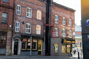 Um edifício de tijolos com várias janelas, uma placa com 'Thomas House' indicando que se trata de um prédio de apartamentos de luxo, e um restaurante 'Kebab Lab' com cardápio visível.