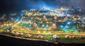 Acampamento numa encosta com várias tendas e estruturas iluminadas.