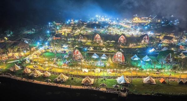 Acampamento numa encosta com várias tendas e estruturas iluminadas.