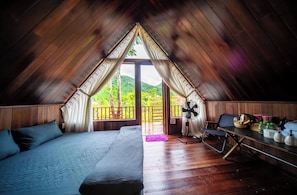 Um quarto de sótão aconchegante com uma cama, uma mesa com objetos e vista para o verde lá fora.
