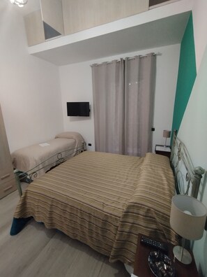 Quarto com cama, televisão, cortina, abajur e controle remoto.