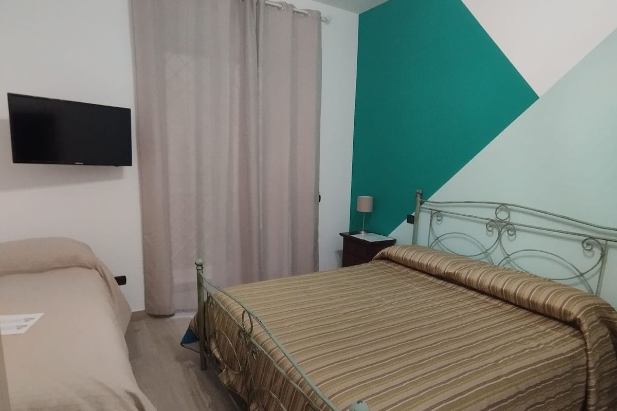 Quarto com cama, televisão, mesa de cabeceira e janela com cortinas.