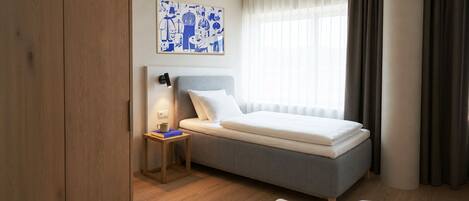 Quarto de hotel com cama, mesa de cabeceira, luminária, janela com cortinas e uma obra de arte na parede.