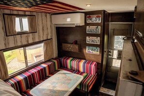 Interior acolhedor de uma RV com área de assentos em bancos listrados, uma mesa para mapas e várias placas de estado na parede.
