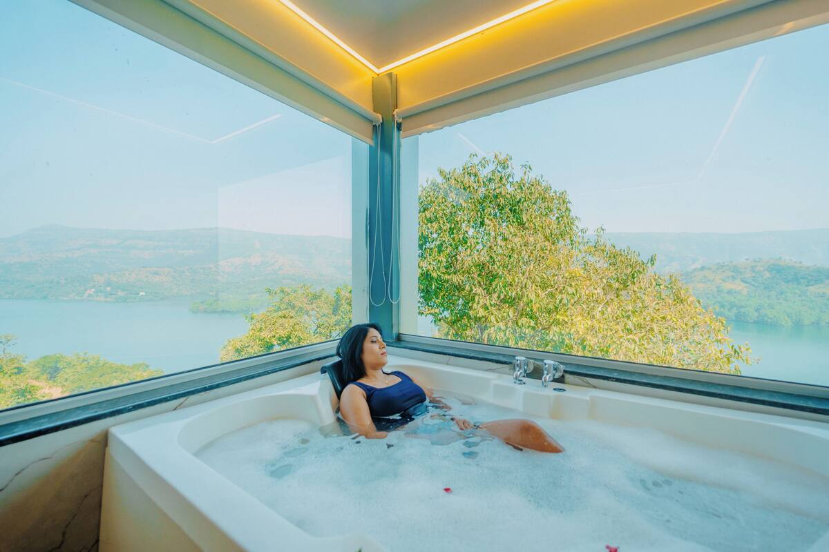 Uma pessoa relaxando em uma banheira com vista para um lago e colinas.