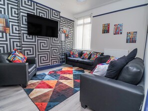 Uma sala de estar moderna com um sofá de couro preto, um tapete geométrico colorido, uma TV de tela plana na parede e arte abstrata nas paredes.