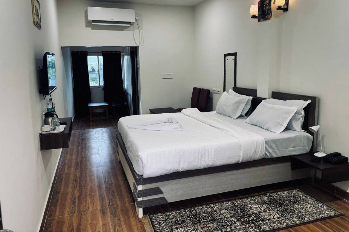 Quarto de hotel moderno com uma cama grande, televisão de tela plana, mesa de cabeceira, ar-condicionado fixado na parede e um tapete estampado.