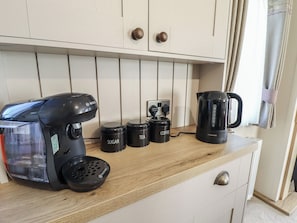 Cozinha com cafeteira, recipientes de açúcar e chá, e chaleira em bancada de madeira.