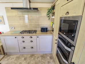 Uma cozinha compacta com fogão a gás, micro-ondas e forno, armários de madeira e painel de azulejos.