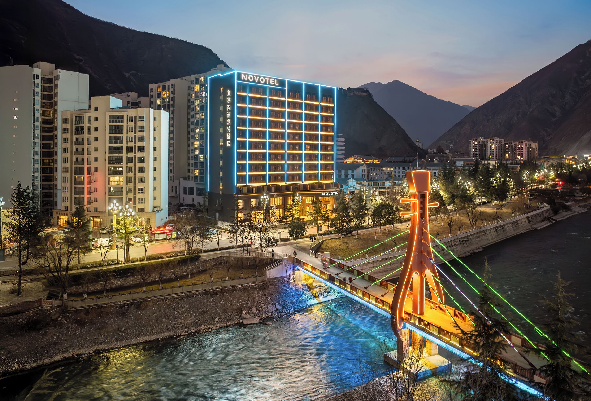 Um hotel com design moderno, uma placa de destaque e vista para um rio e montanhas.