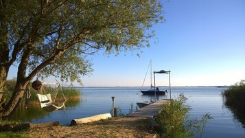 Um lago tranquilo com um píer, um barco e uma rede sob uma árvore.