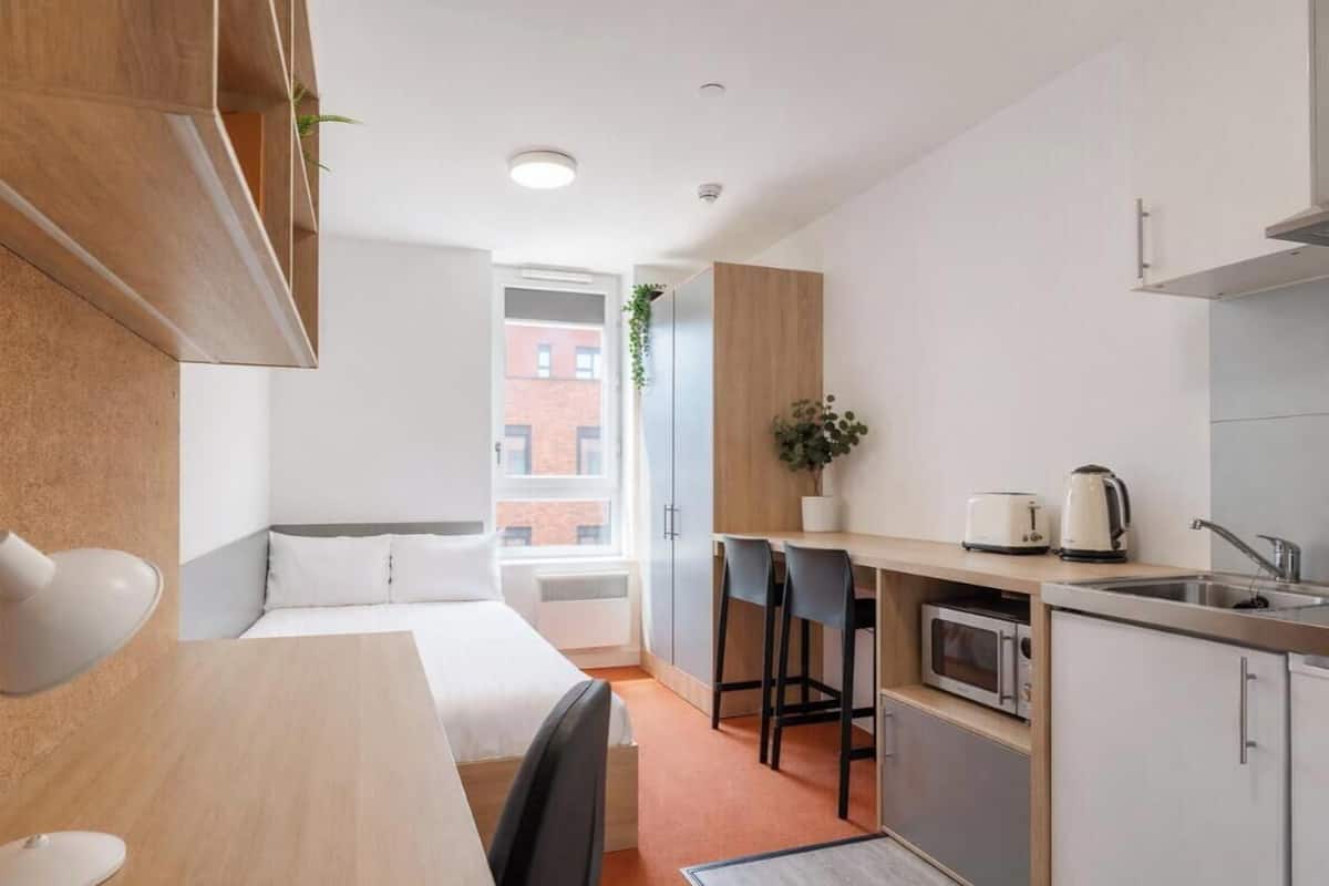 Quarto de hotel moderno com cama, escrivaninha, cozinha compacta e vista para a cidade.