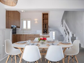 Uma cozinha moderna com armários de madeira, uma mesa de jantar posta para quatro pessoas e uma escadaria.