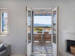 Quarto com porta de vidro deslizante que dá para um pátio externo com móveis de vime e vista para o mar.