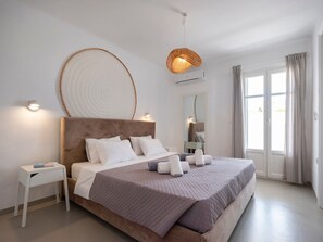 Quarto moderno com cama grande, mesas de cabeceira, luminária fixada na parede e janela com cortinas.