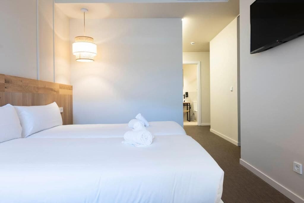 Quarto de hotel com uma cama grande, televisão de tela plana na parede e um corredor que dá para outros quartos.