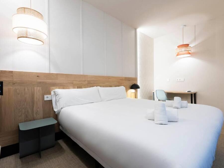 Quarto de hotel com uma cama grande, mesas de cabeceira, uma escrivaninha e duas luzes pendentes.