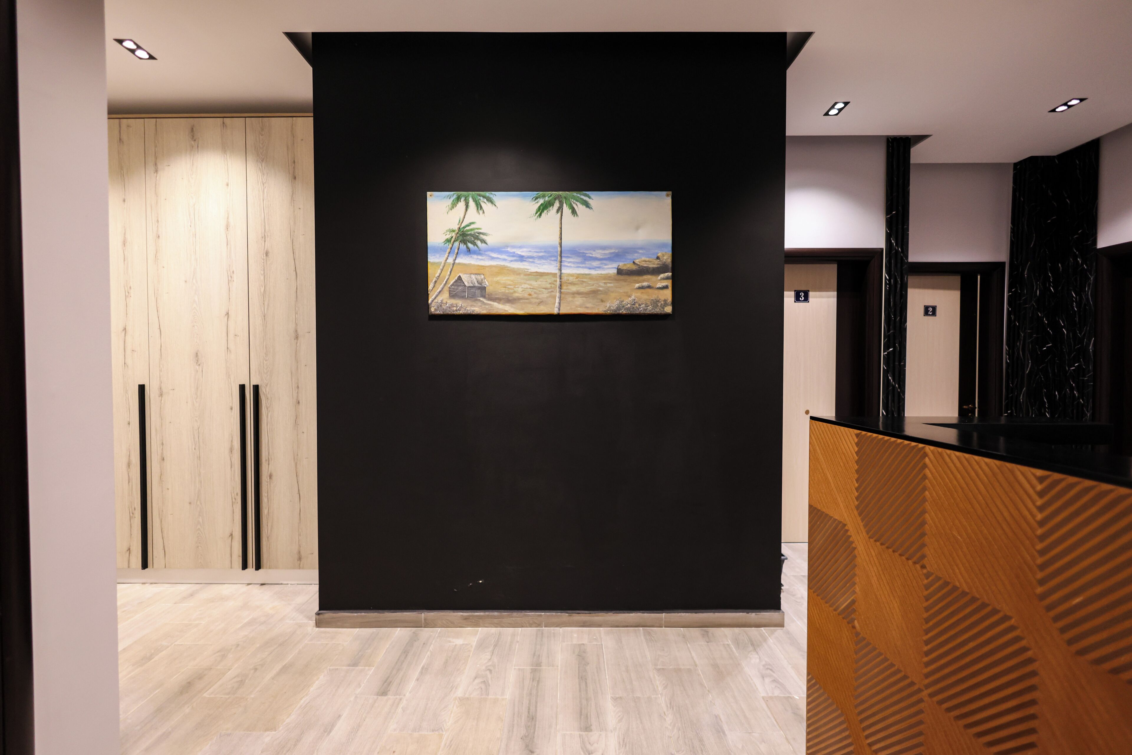 Um saguão de hotel com piso de madeira, uma pintura de uma praia e um balcão de recepção.