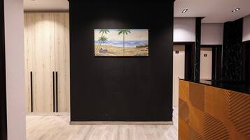 Um saguão de hotel com piso de madeira, uma pintura de uma praia e um balcão de recepção.