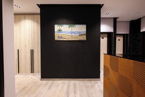 Um saguão de hotel com piso de madeira, uma pintura de uma praia e um balcão de recepção.