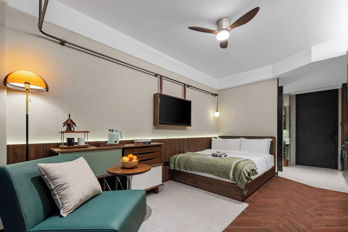 Quarto de hotel moderno com cama, sofá, televisão e ventoinha no teto.