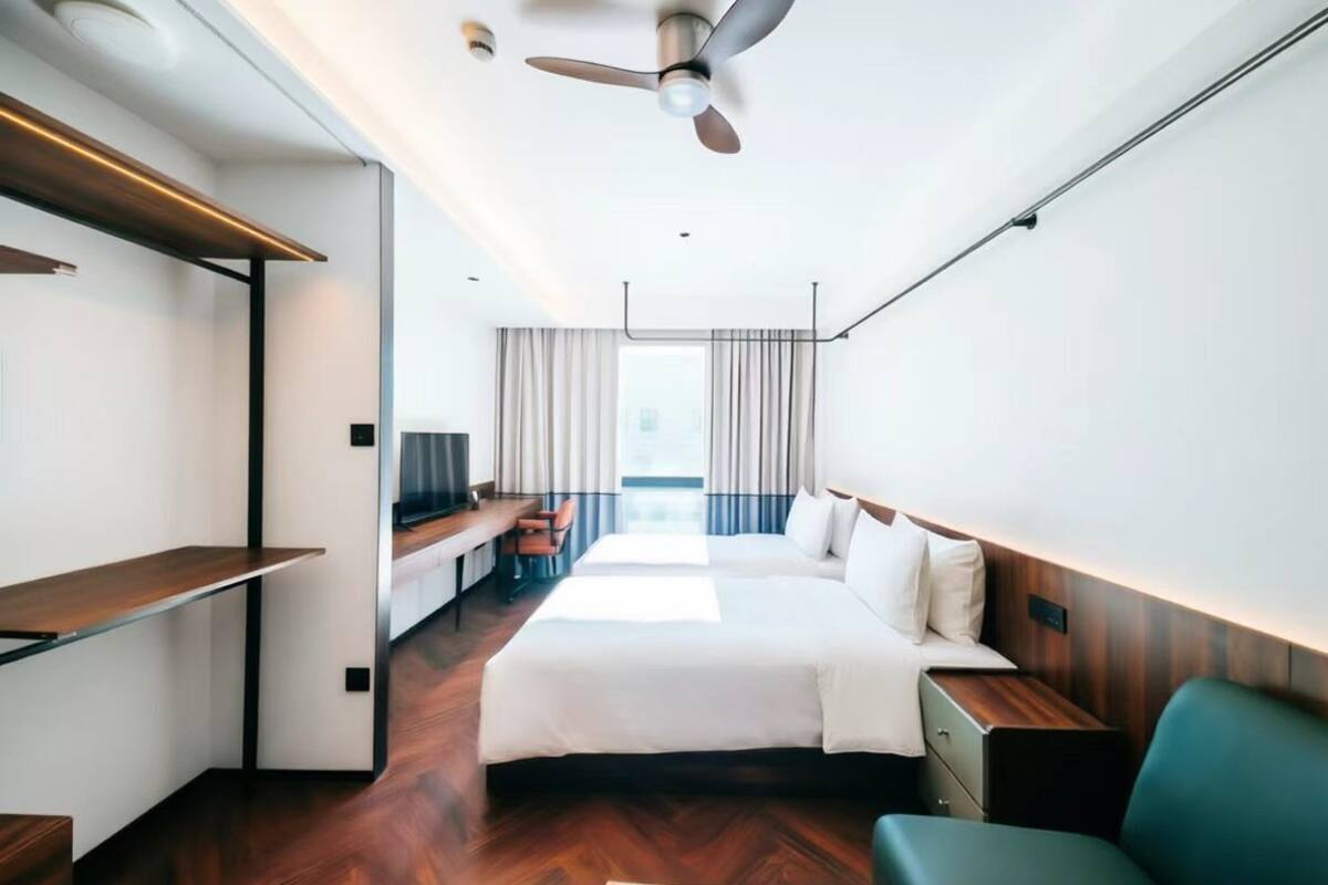 Quarto de hotel moderno com uma cama, uma escrivaninha, uma cadeira, uma televisão e um ventilador de teto.