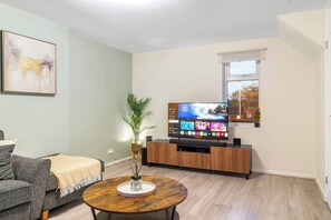 Uma sala de estar com sofá, mesa de centro, televisão sobre suporte de madeira e um quadro na parede.