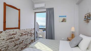 Quarto de hotel com parede de tijolos, cama com roupa de cama branca, espelho com moldura de madeira, janela com vista e uma pequena mesa com abajur.