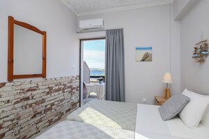 Quarto de hotel com parede de tijolos, cama com roupa de cama branca, espelho com moldura de madeira, janela com vista e uma pequena mesa com abajur.