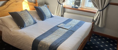 Uma cama bem arrumada com colcha azul e branca, cabeceira de madeira e mesa de cabeceira com abajur.