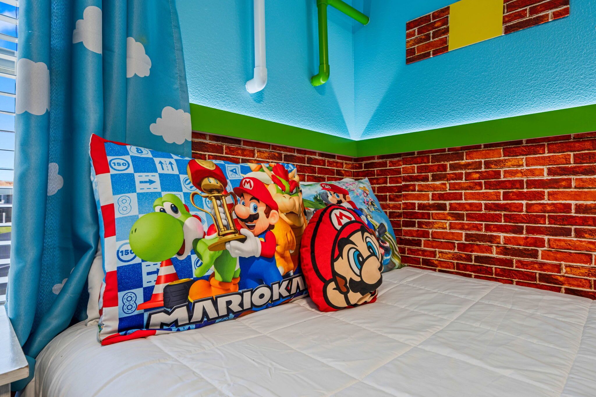 Uma cama com um travesseiro e outro travesseiro temáticos do Mario sobre um colchão branco.