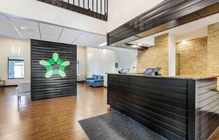 Uma área de recepção com design moderno, apresentando um balcão de atendimento, um espaço de espera com sofá e um logotipo grande na parede.