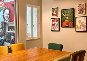 Uma área de refeições com uma mesa de madeira, cadeiras verdes e amarelas, e obras de arte na parede.