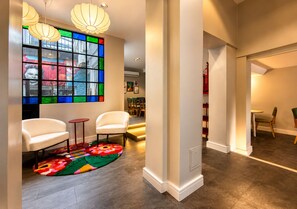 Um interior moderno com uma grande janela de vitrais, cadeiras brancas, um tapete colorido e iluminação pendente.