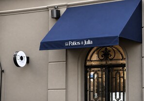 Entrada de um prédio com toldo azul identificado como 'Los Patios de Julia' e uma placa circular com 'DOT Boutique' na parede.