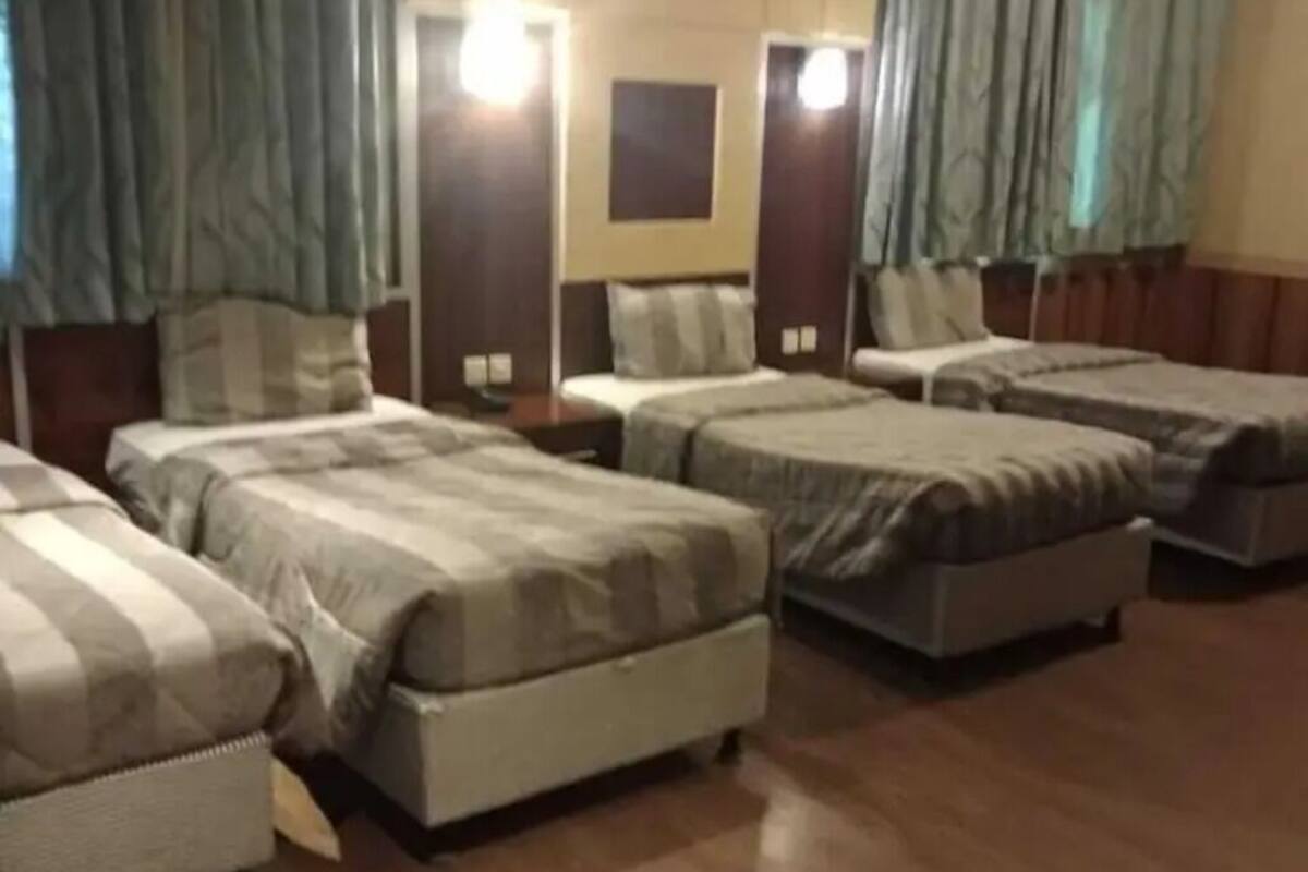 Quarto de hotel com quatro camas dispostas em linha, piso de madeira e um espelho grande na parede.