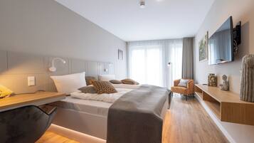 Quarto de hotel moderno com cama, escrivaninha, cadeira e televisão.