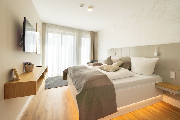 Quarto moderno com cama, mesas de cabeceira, televisão e janela com cortinas.